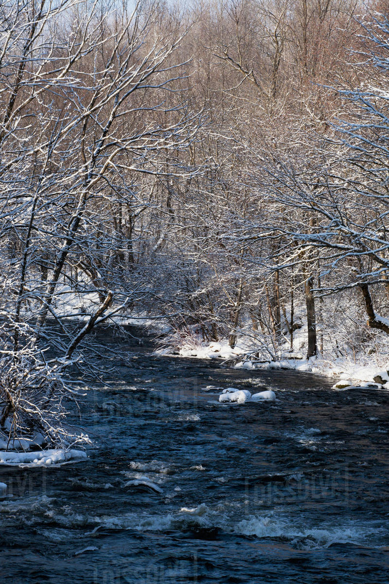 Water flowing in a river with snow covered shoreline; Fulford, Quebec ...