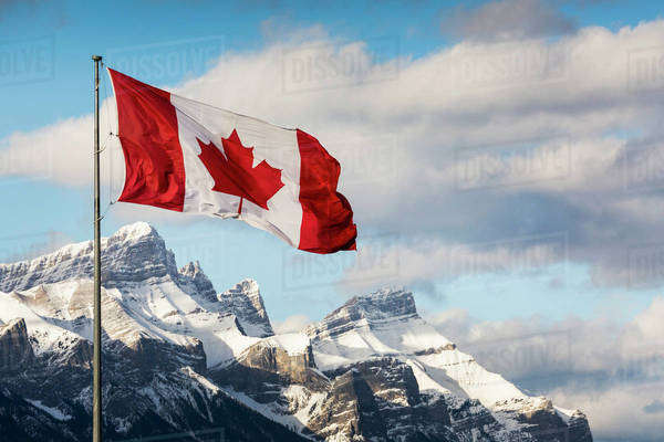 Canadian flag blowing in the wind on a flag pole with snow covered ...