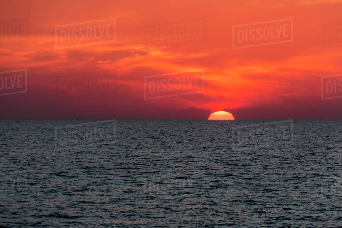Dramatic red sky with the sun setting under the ocean and horizon ...