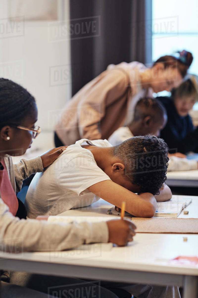 Teenage girl consoling depressed male student resting head on desk in ...