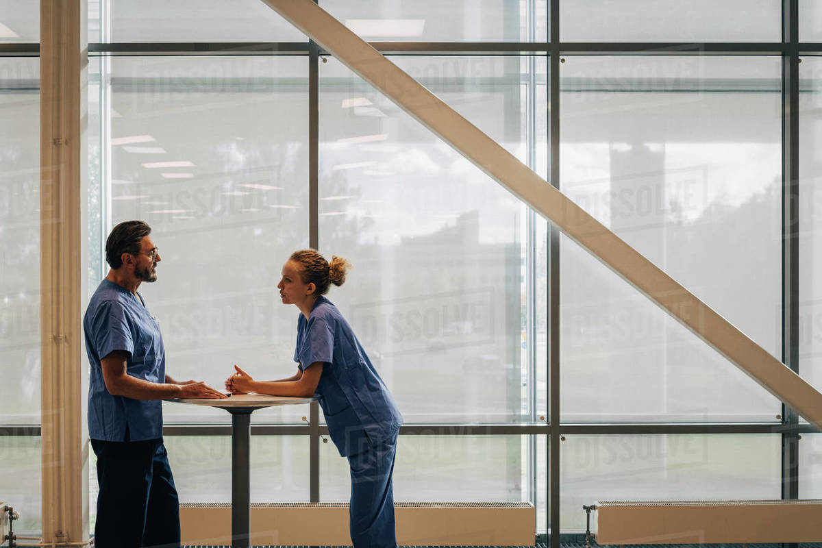 Side view of hospital staff discussing while standing by window in ...