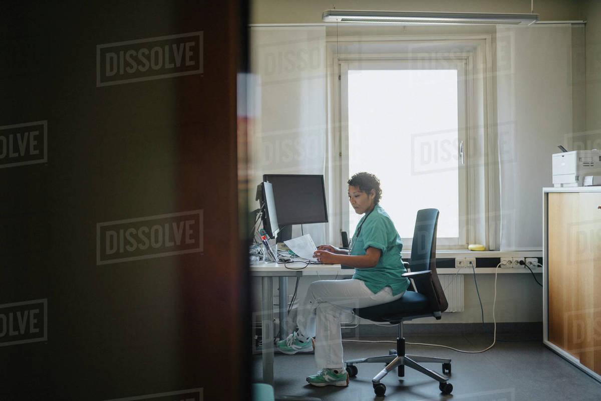 Side view of female doctor checking medical record while sitting at ...