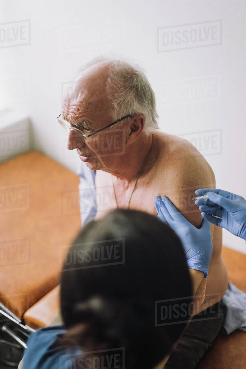 Shirtless male senior patient taking vaccination on arm at hospital ...