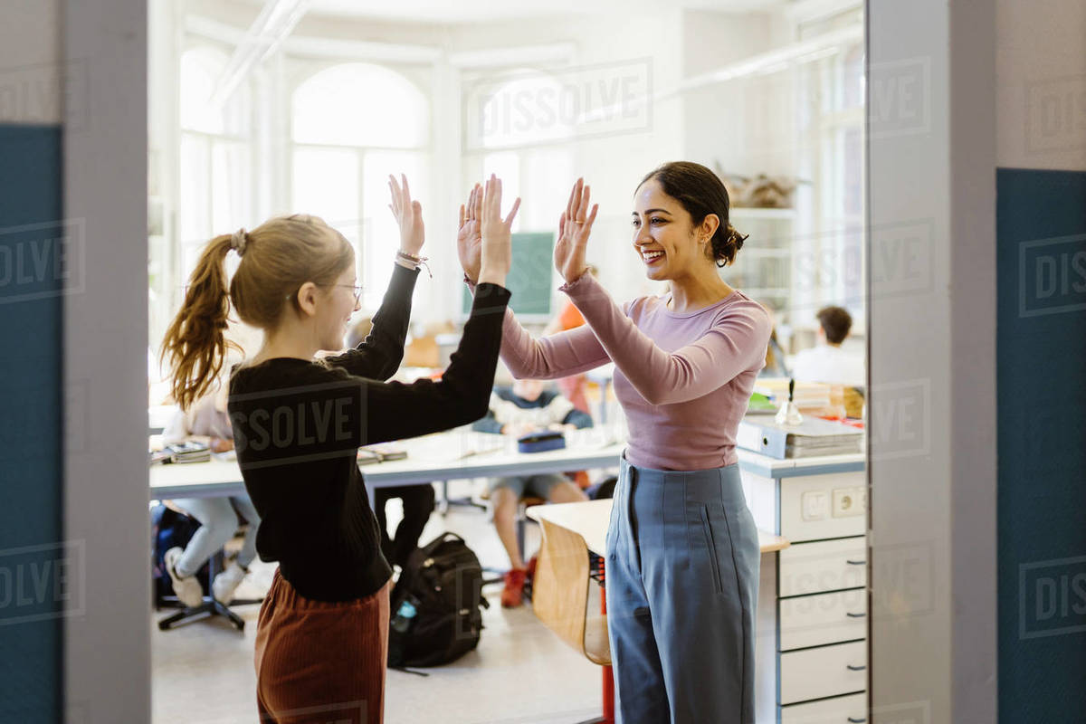 Smiling female teacher giving high-five to girl standing in classroom ...