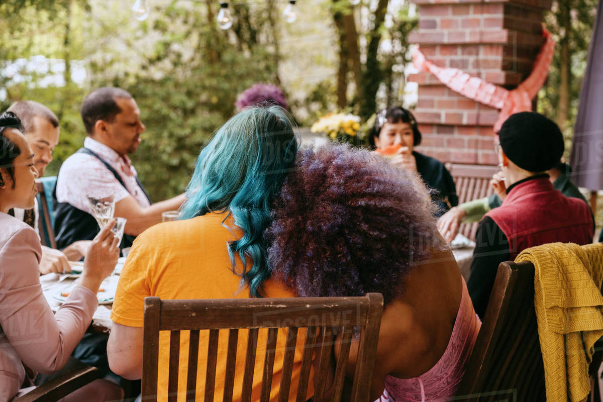 Rear view of LGBTQ friends sitting together during dinner party in back ...