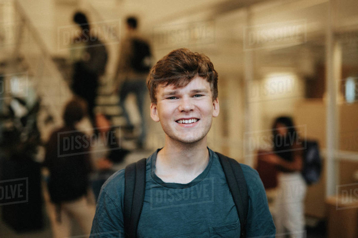 Portrait of cheerful young male student standing in university - Stock ...