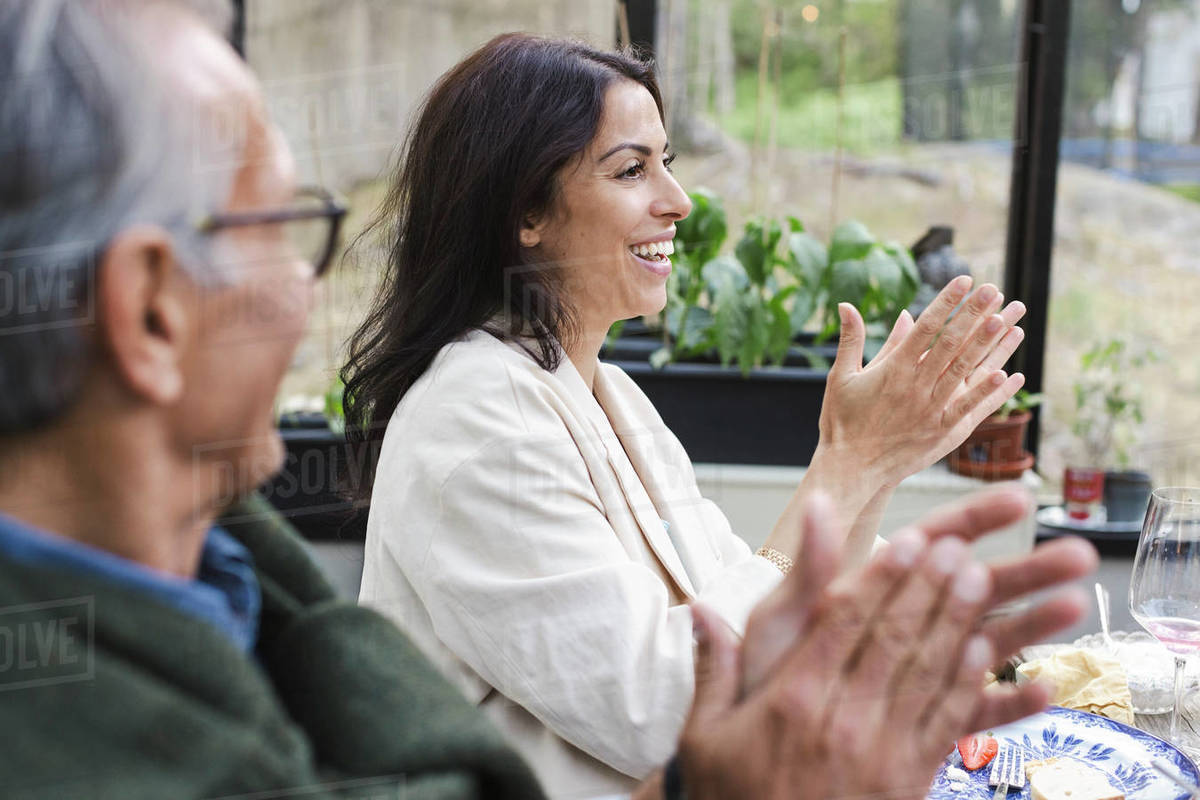Side view of happy man and woman clapping while sitting at patio during ...
