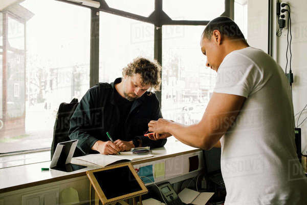 Male customer writing details while standing at checkout counter with ...