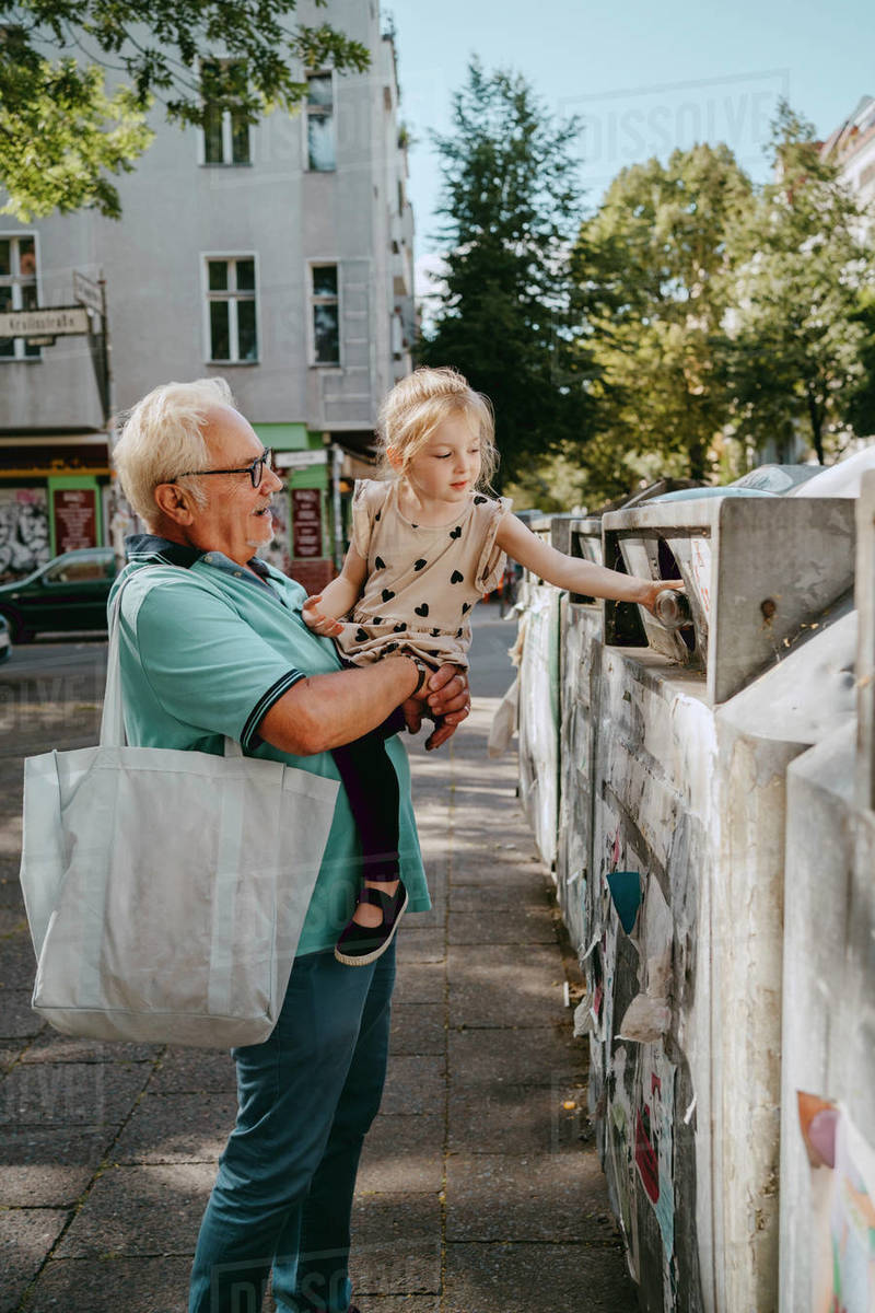 Grandfather carrying daughter trashing garbage while standing at street ...