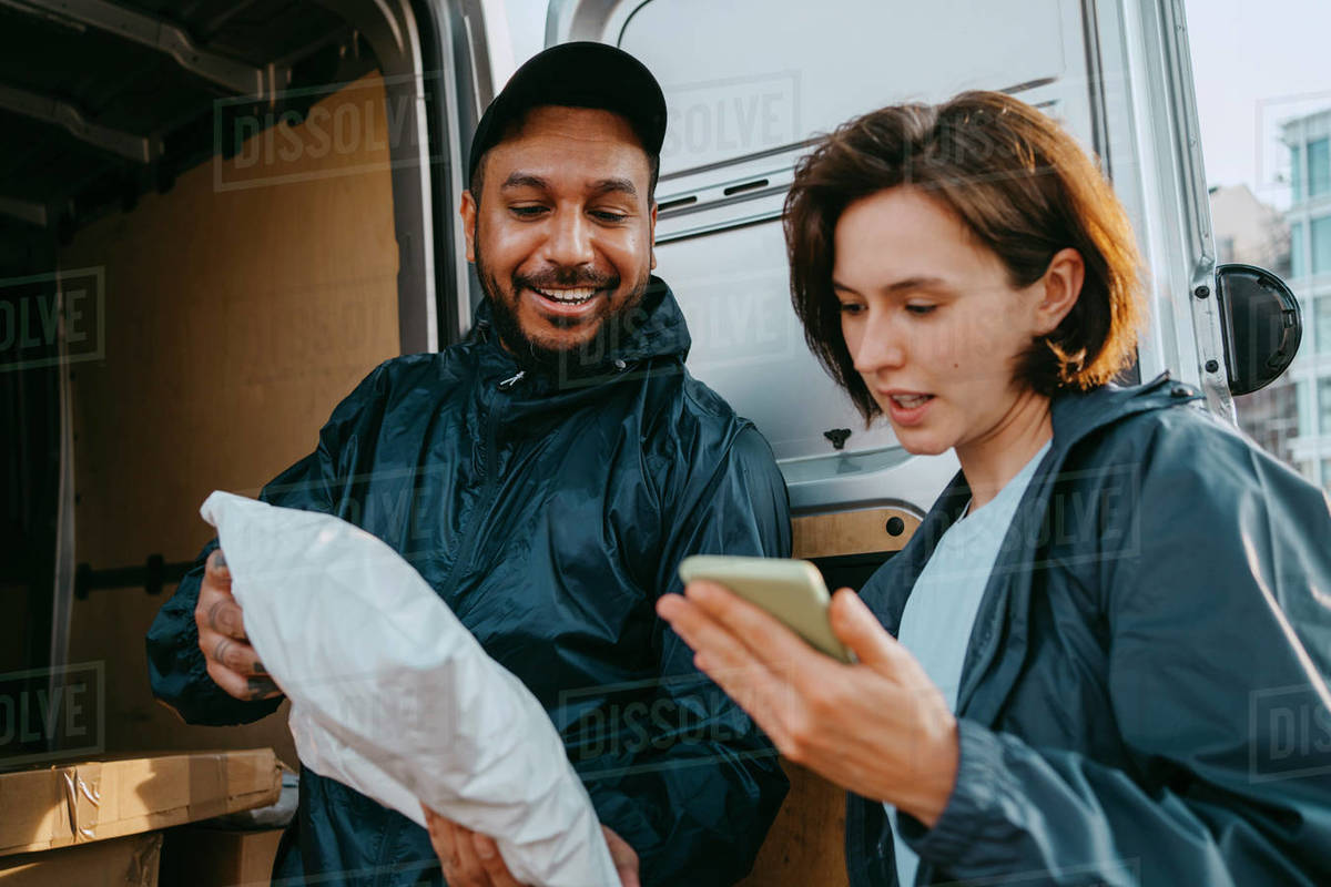 Smiling male delivery person showing parcel to female coworker holding ...