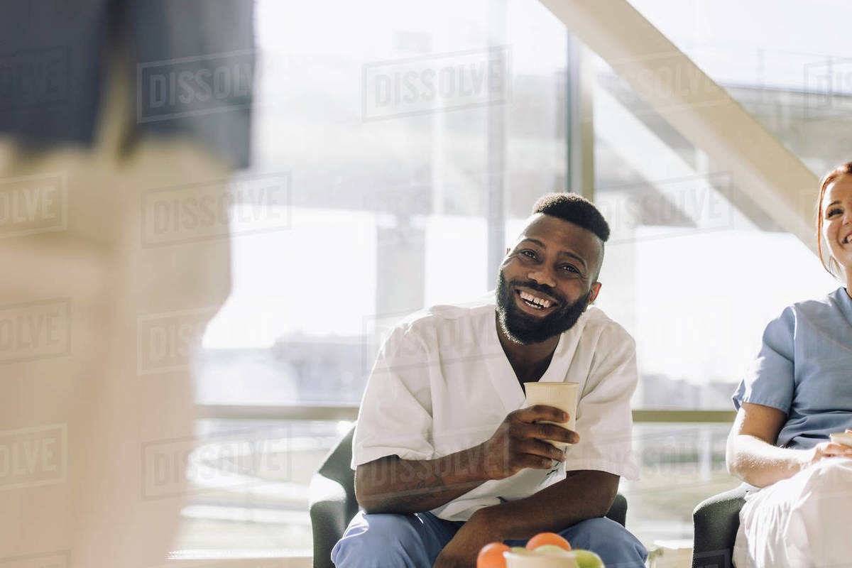 Happy male doctor laughing while holding disposable cup in hospital ...