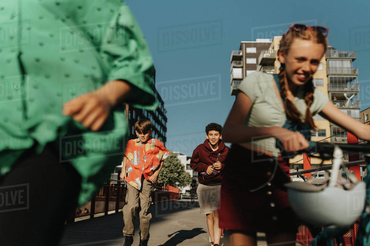 Male friends running on street while female friend walking with bicycle ...