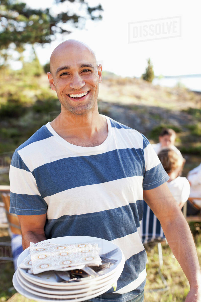 Cheerful man holding plates with friends in background - Stock Photo ...
