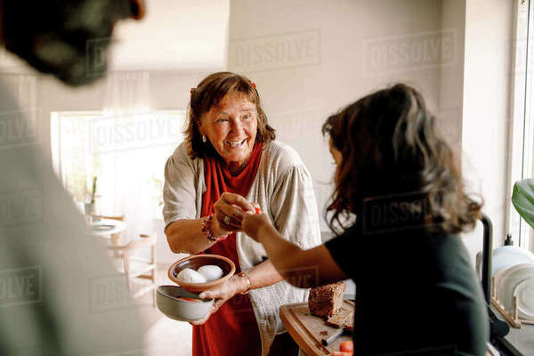 Smiling senior woman giving cherry tomato to grandson in kitchen at ...