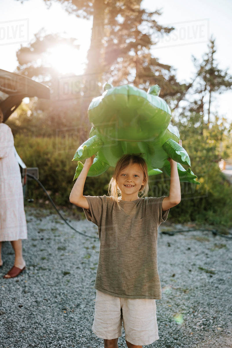 Portrait of smiling boy carrying crocodile swimming float overhead ...