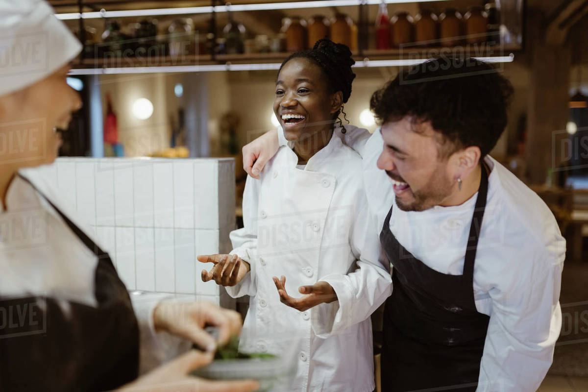 Cheerful male chef with arm around female colleague enjoying at ...
