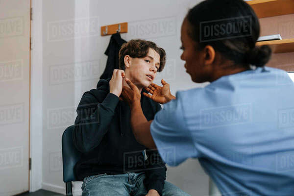 Female doctor checking neck of patient while sitting in medical ...