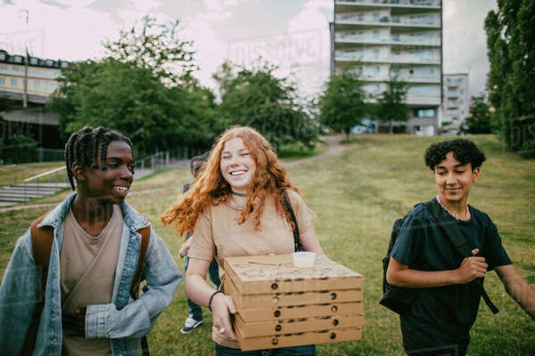 Happy teenage girl carrying pizza boxes while walking with friends in ...
