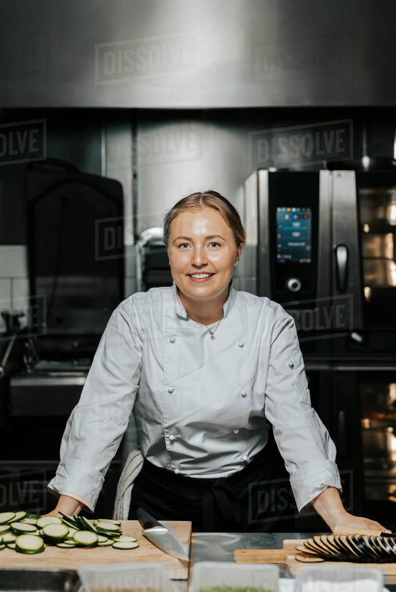 Portrait of smiling female chef wearing white uniform and leaning on ...
