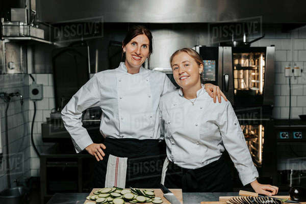 Smiling female chef standing with arm around colleague in commercial ...