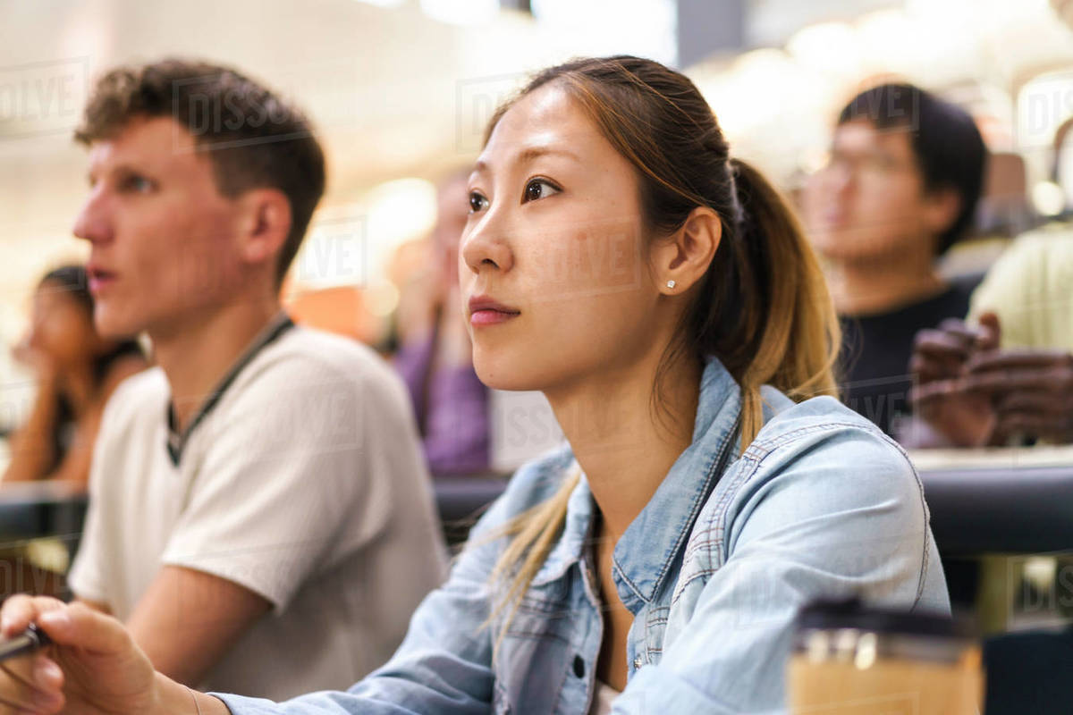 Female student looking away while sitting in lecture hall at university ...