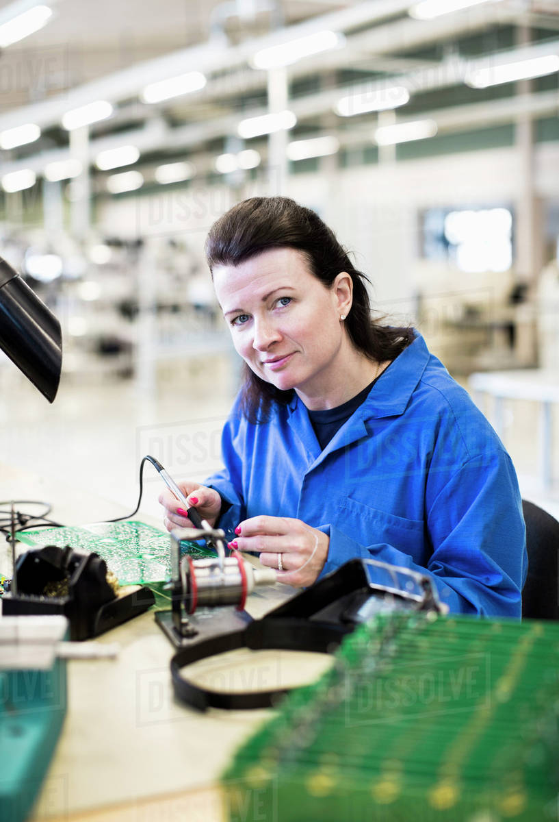 Portrait of female electrician working on circuit board at desk in ...