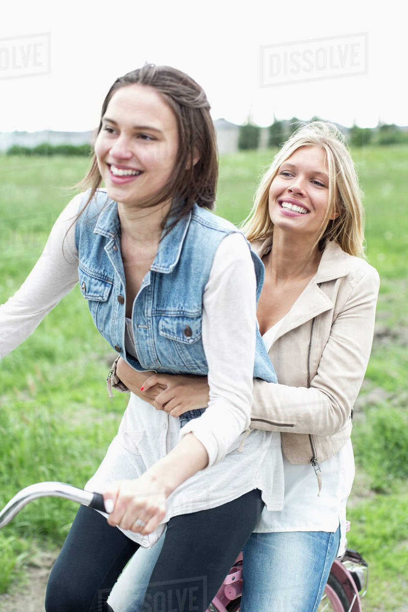 Happy female friends enjoying bicycle ride on country road - Royalty ...