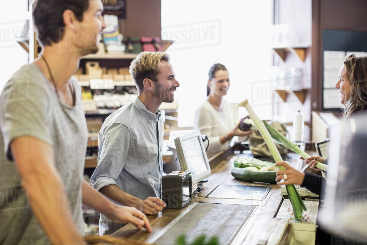Happy friends looking at cashier at checkout counter in grocery store ...