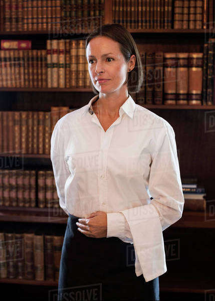 Confident waitress standing against bookshelf in restaurant - Stock ...