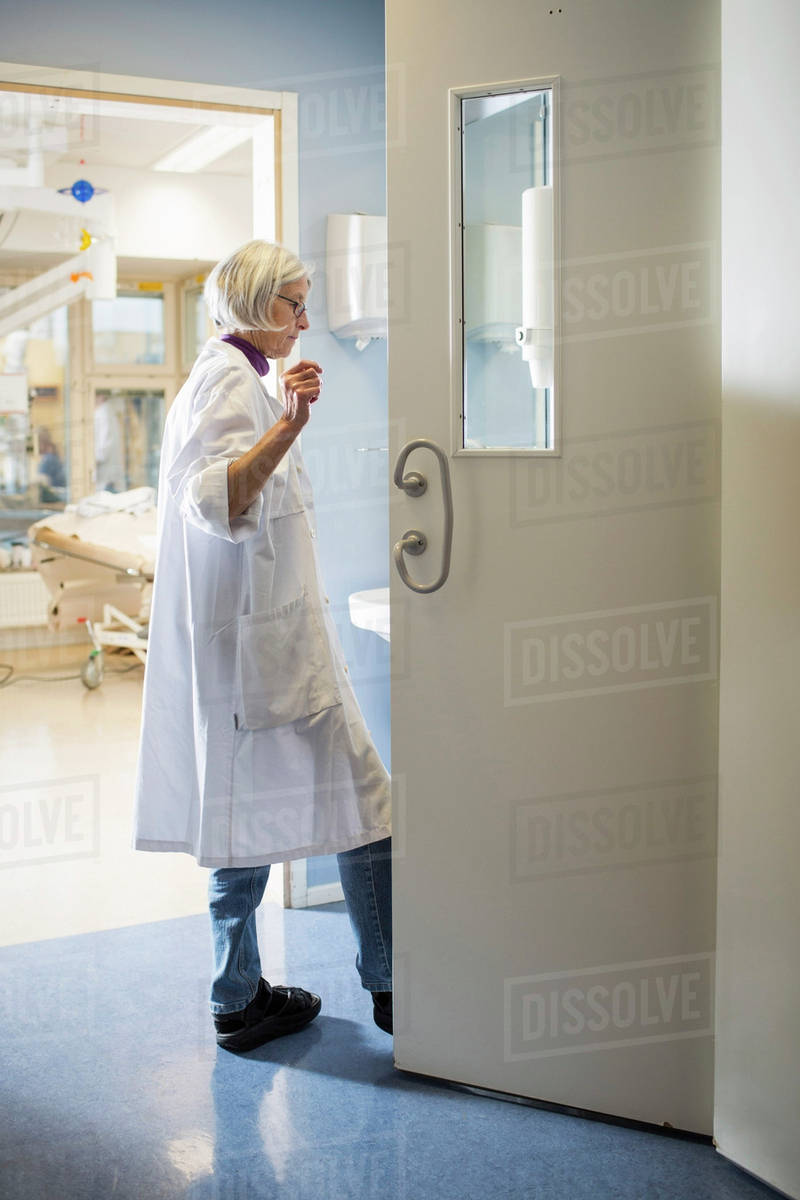 Full length side view of senior female doctor entering hospital ...