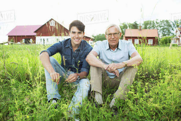 Full length portrait of grandfather and grandson sitting on grassy ...