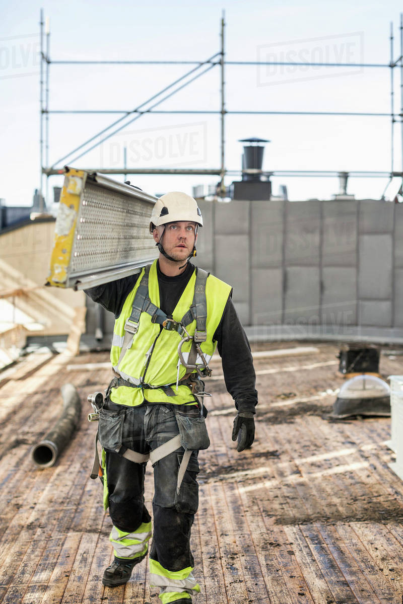 Construction worker carrying metal plank at site - Stock Photo - Dissolve