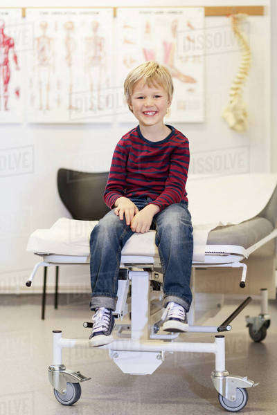 Portrait of happy boy sitting on examination table in orthopedic clinic ...
