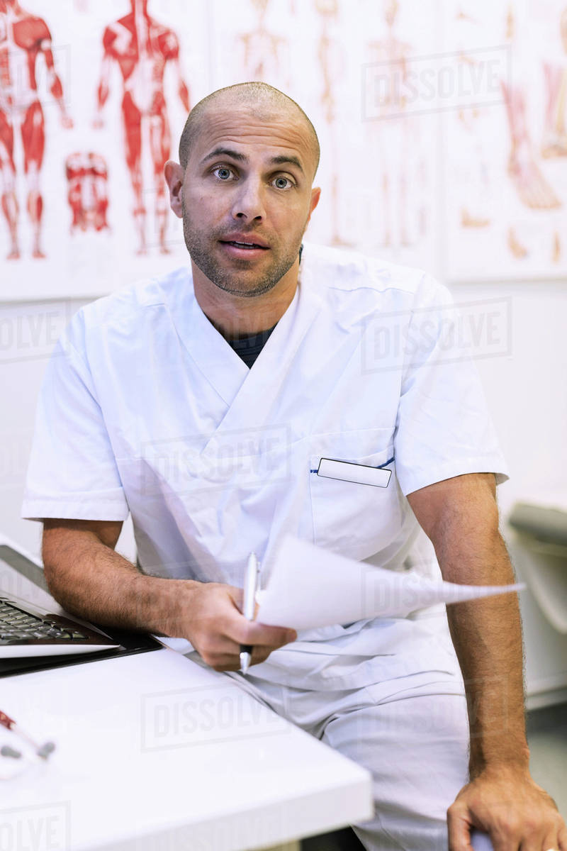 Portrait of male orthopedic doctor holding document at desk in clinic ...