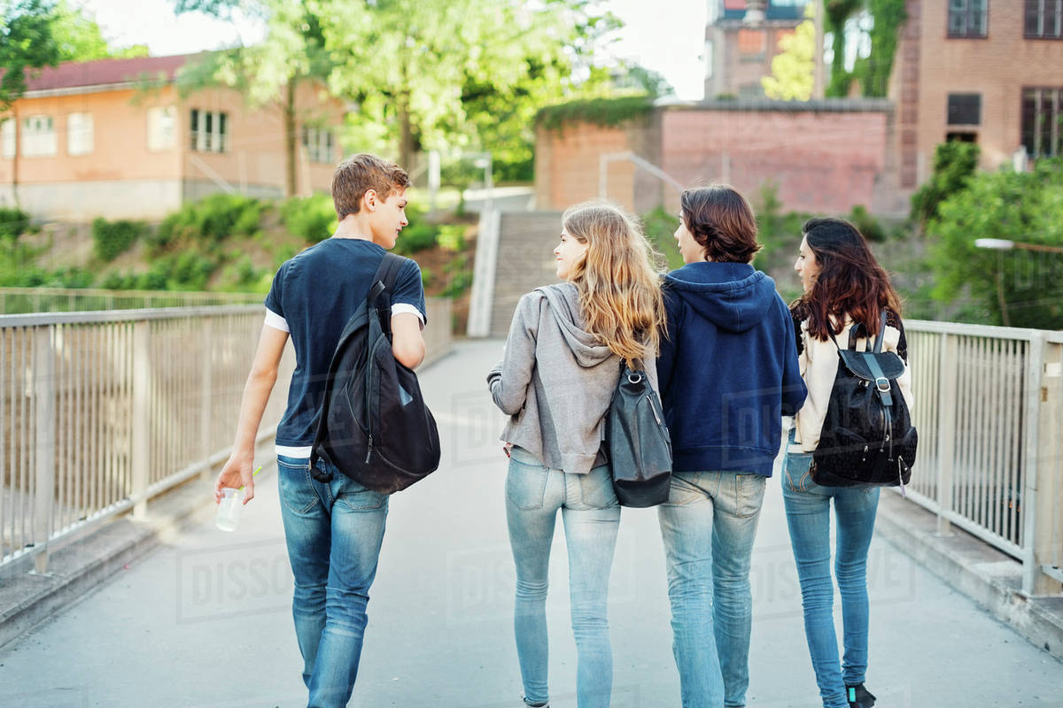 Rear view of teenagers talking while walking on bridge in city ...