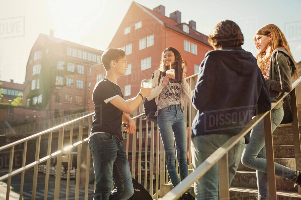Teenagers talking while having drinks on steps in city - Royalty-free ...