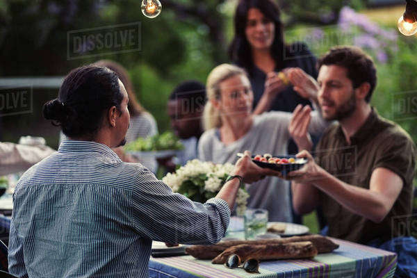 Men passing food at dining table during dinner party at yard - Royalty ...