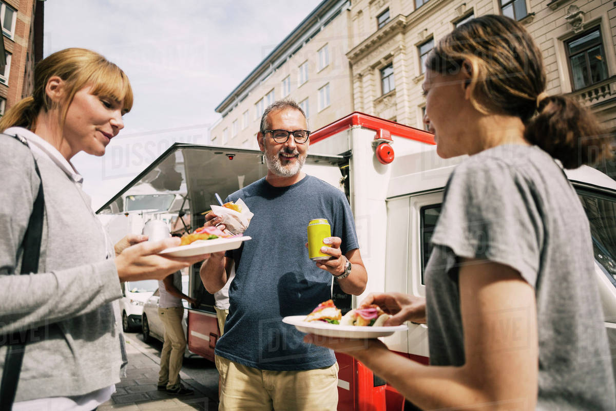 People eating snacks while standing against truck at city - Royalty ...