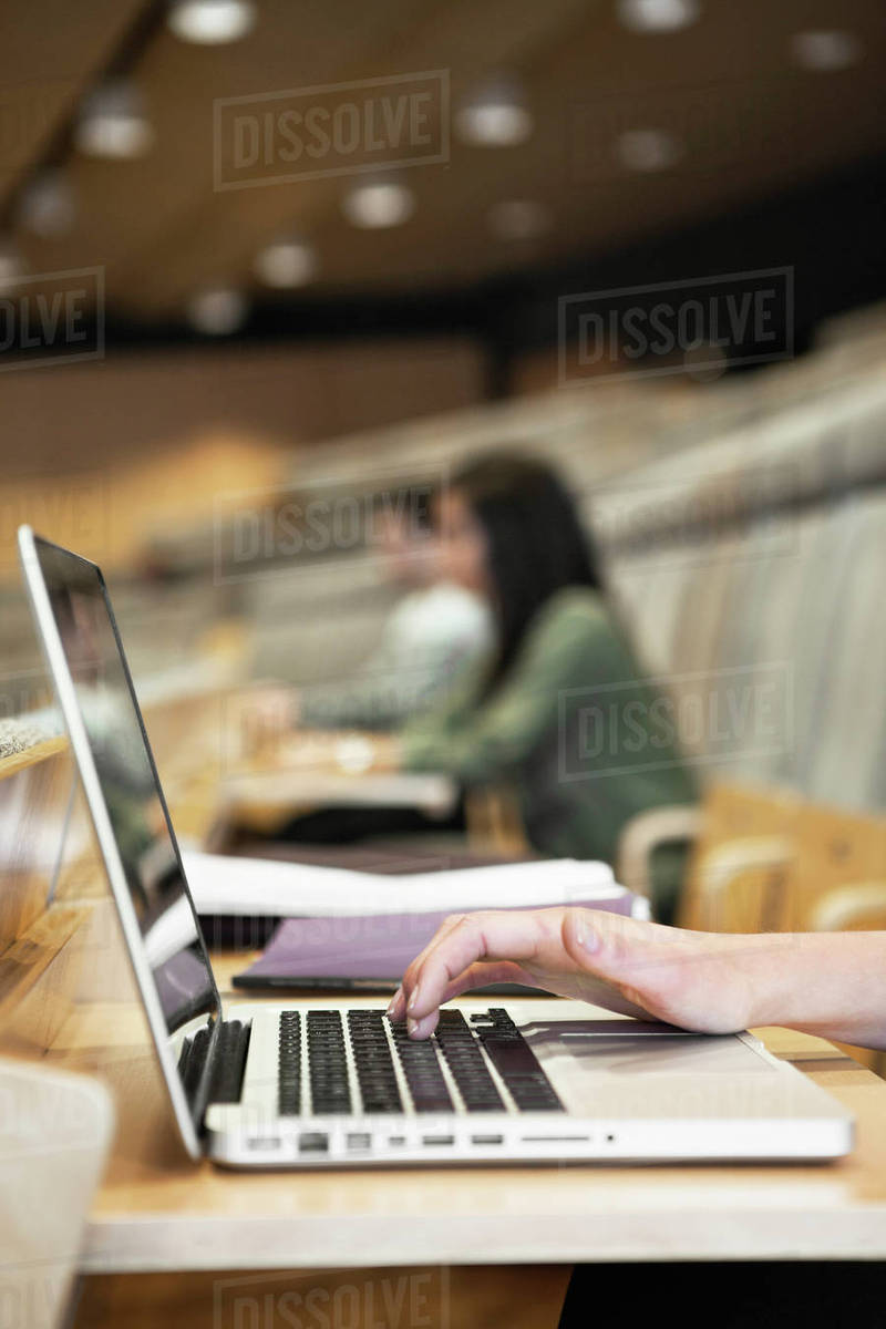 Close-up of human hand typing on laptop keyboard with people in ...