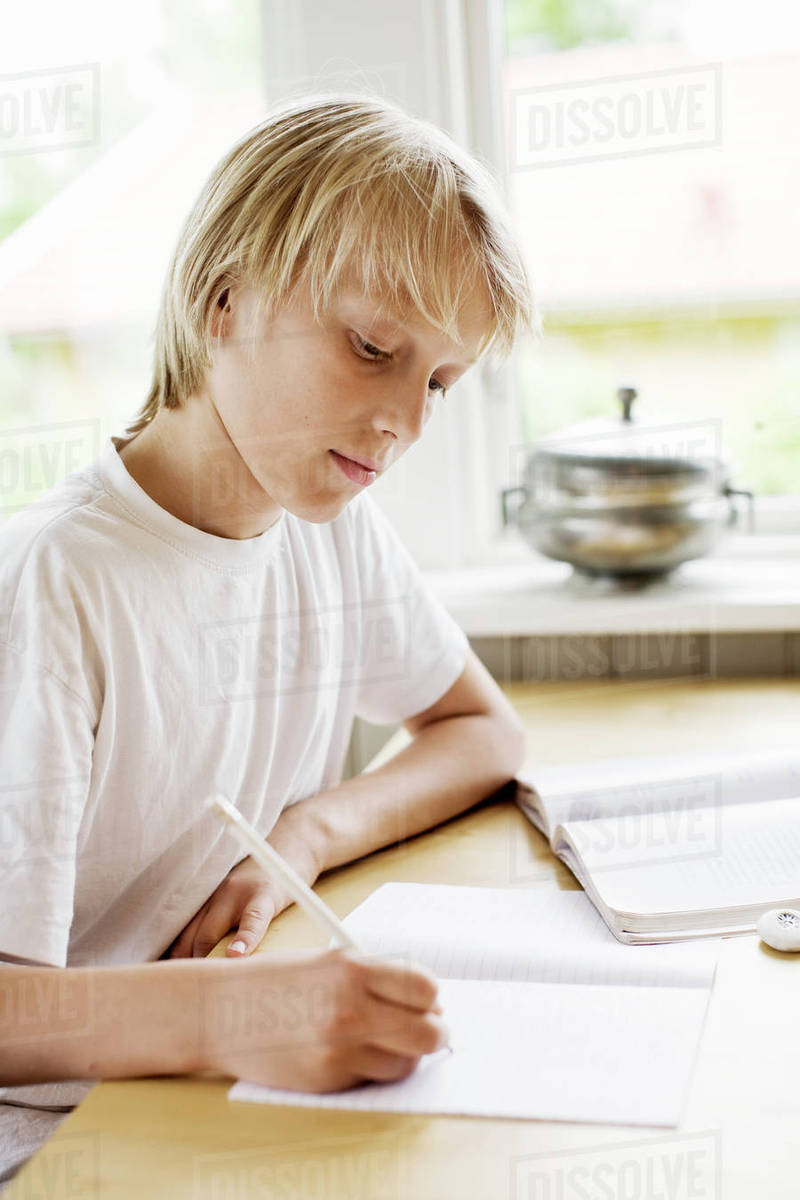 Boy writing in book on table at home - Royalty-free Stock Photo | Dissolve