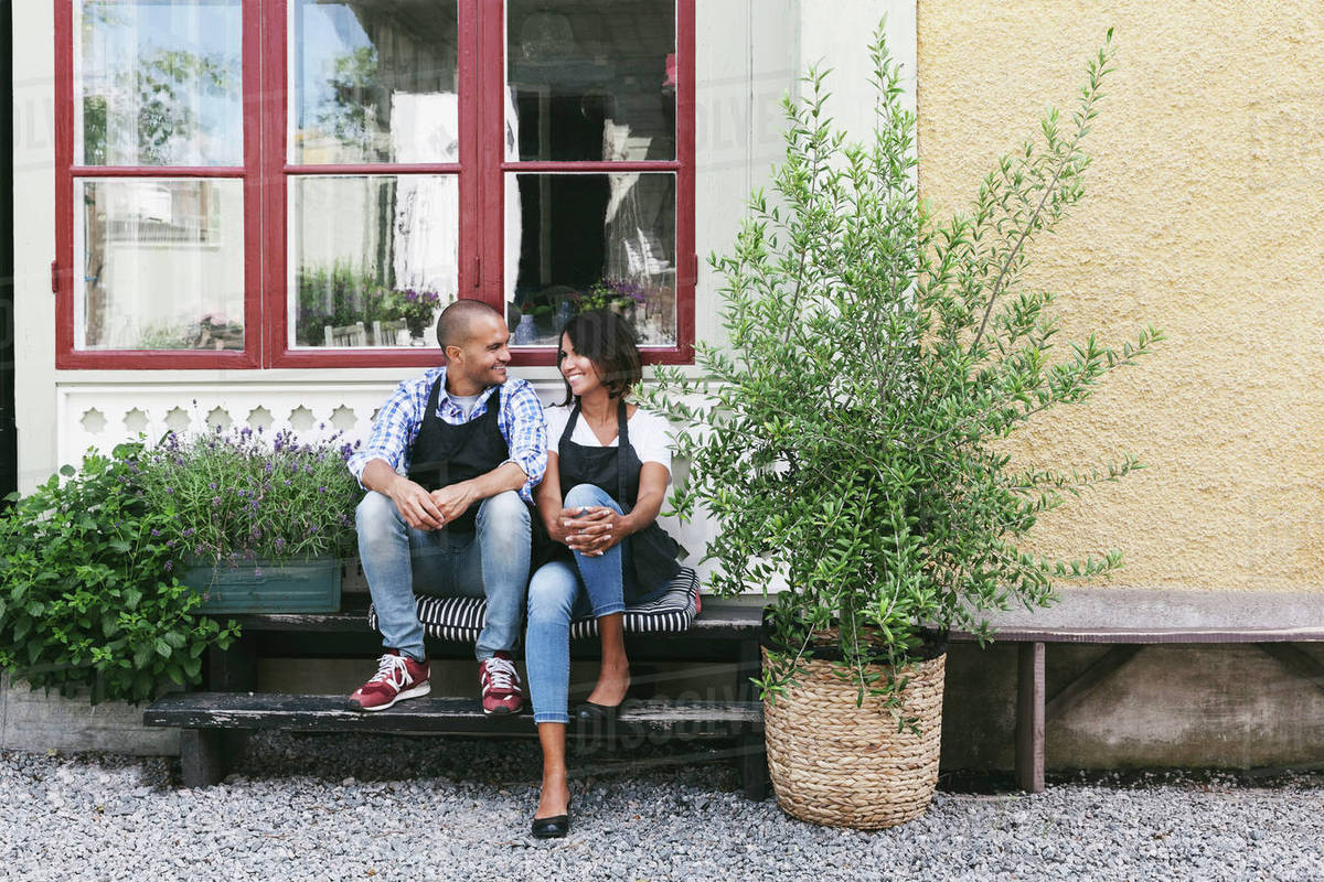 Smiling owners sitting on bench against window outside cafe - Stock ...
