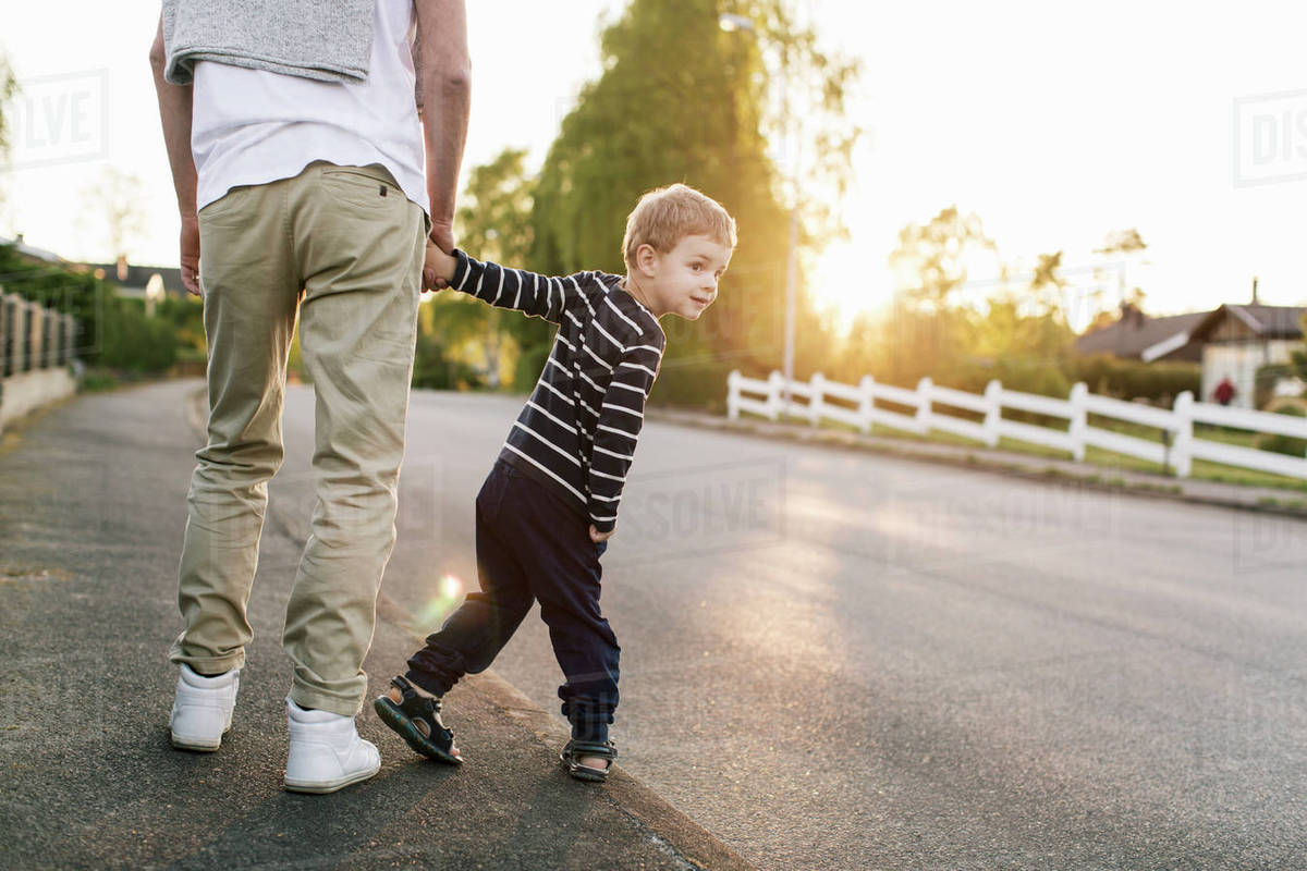 Boy looking over shoulder while walking with father on street - Royalty ...