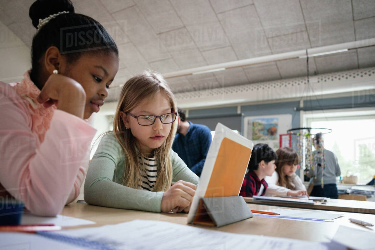 Female students reading digital tablet at desk in classroom - Royalty ...