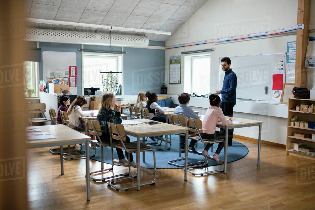 Confident teacher teaching students in classroom at school - Stock ...