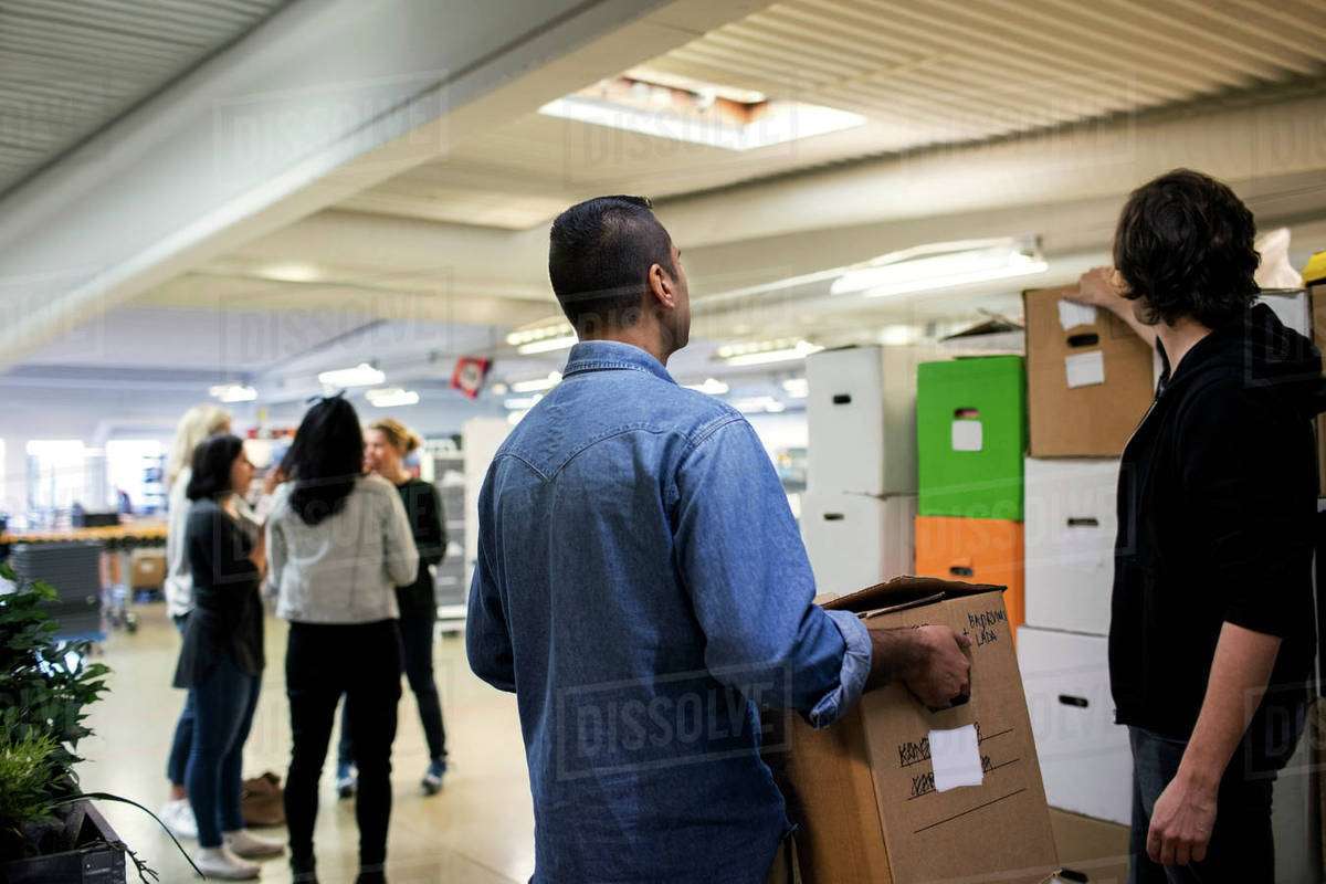 Male volunteers arranging cardboard boxes while colleagues working in ...