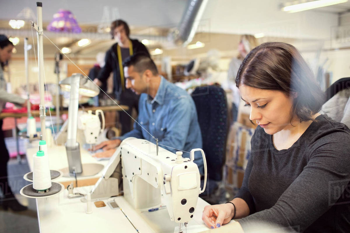 Concentrated woman sewing clothes while volunteers working at workshop ...