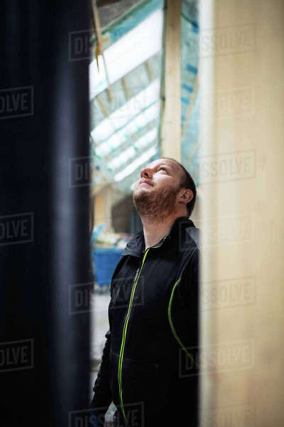 Man in protective clothing looking up while standing at construction ...