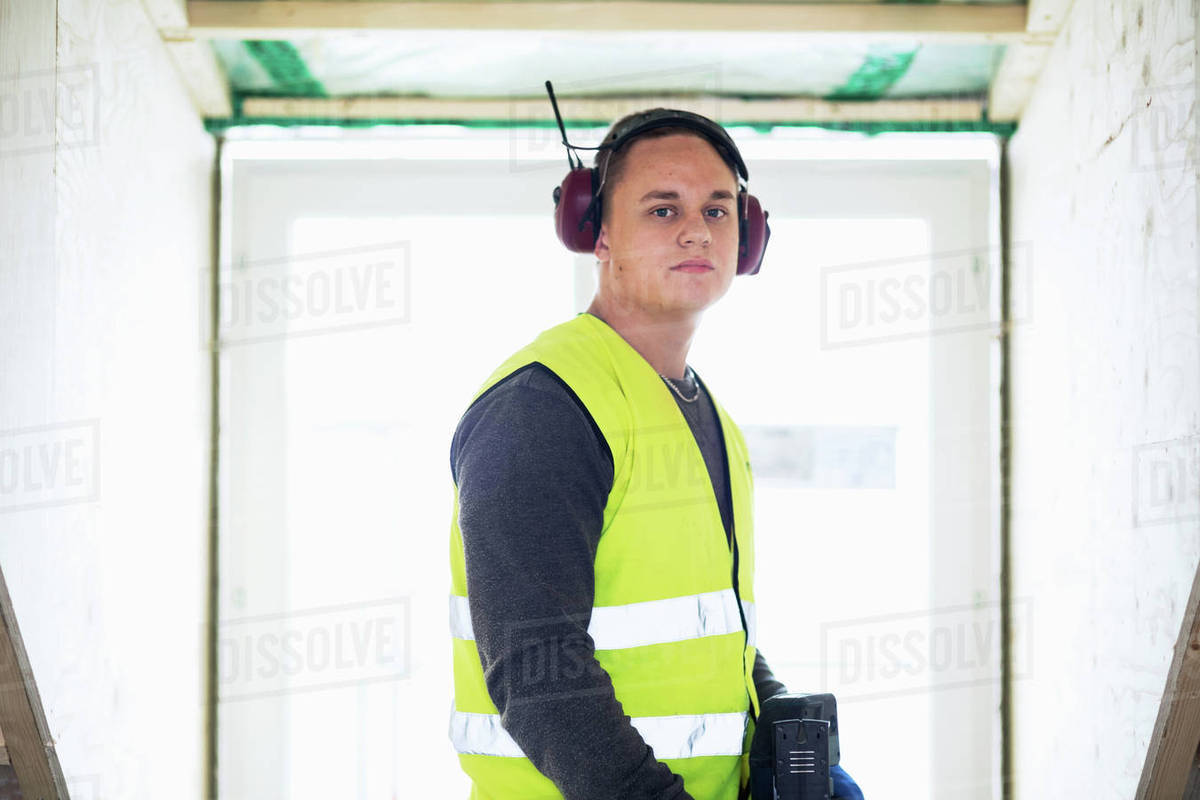 Portrait of serious man wearing ear protectors standing against window ...