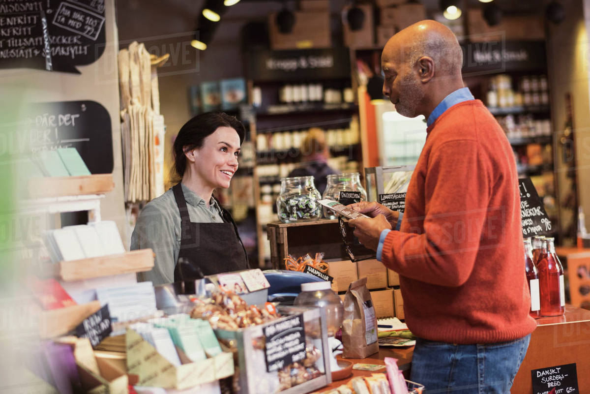 Smiling owner talking to customer holding packet while standing at ...
