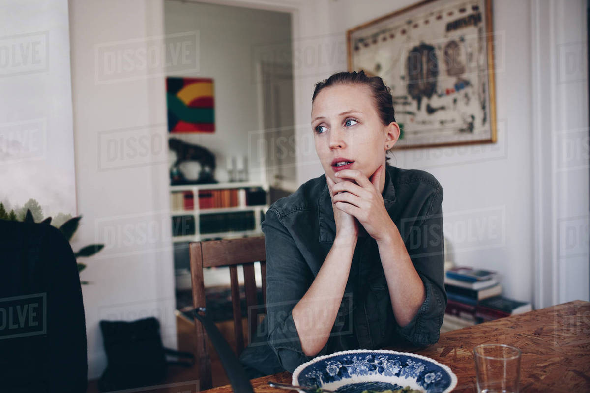 Thoughtful woman sitting at dining table in room - Royalty-free Stock ...